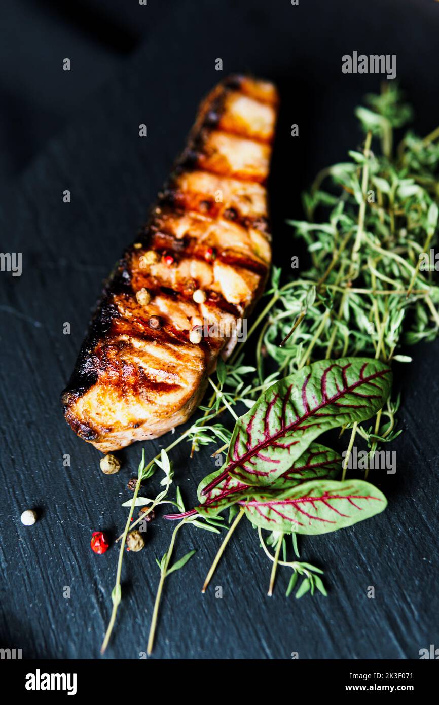 Grilled salmon fish fillet with green salad on the black cutting board ...