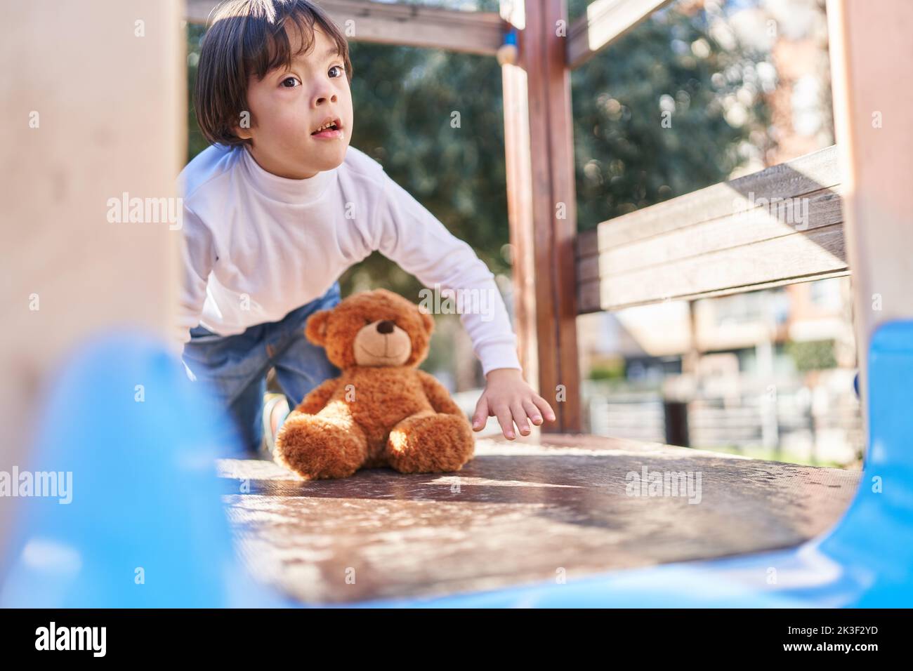 Down syndrome kid smiling confident playing with teddy bear on slide at ...