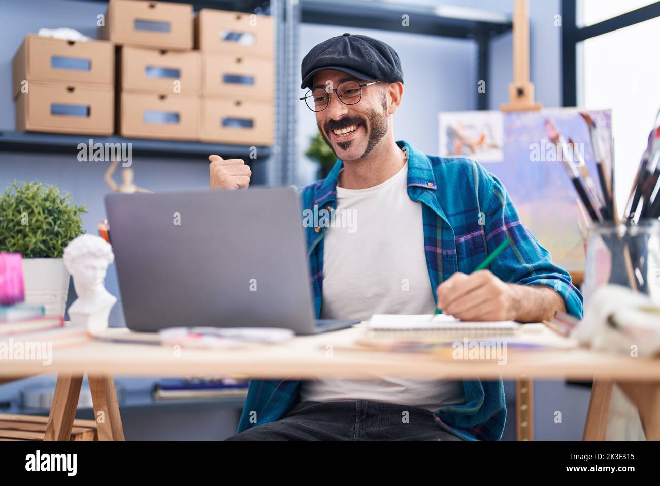 Hispanic man with beard doing online video call at art studio pointing ...