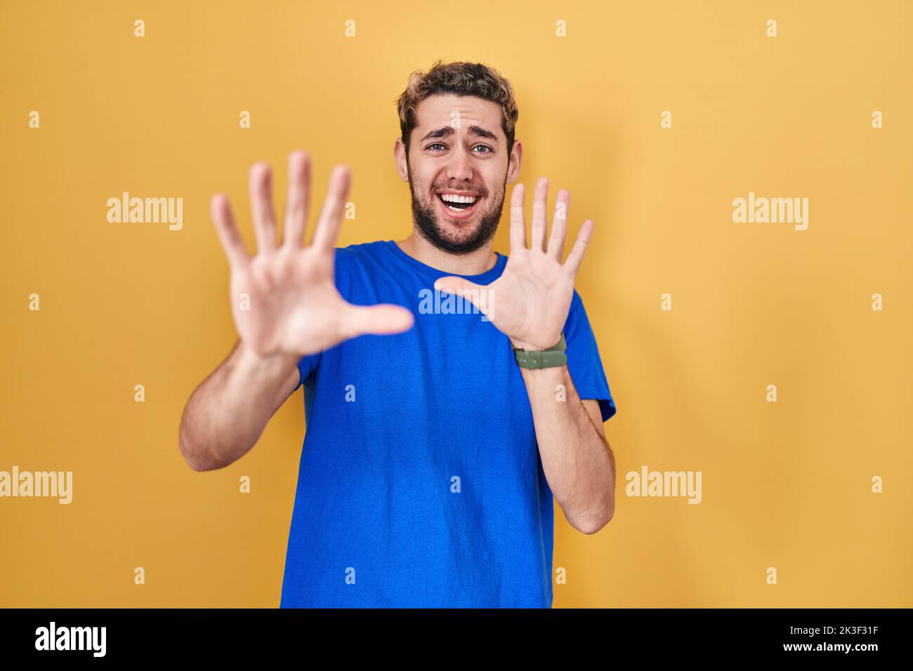 Hispanic man with beard standing over yellow background afraid and ...