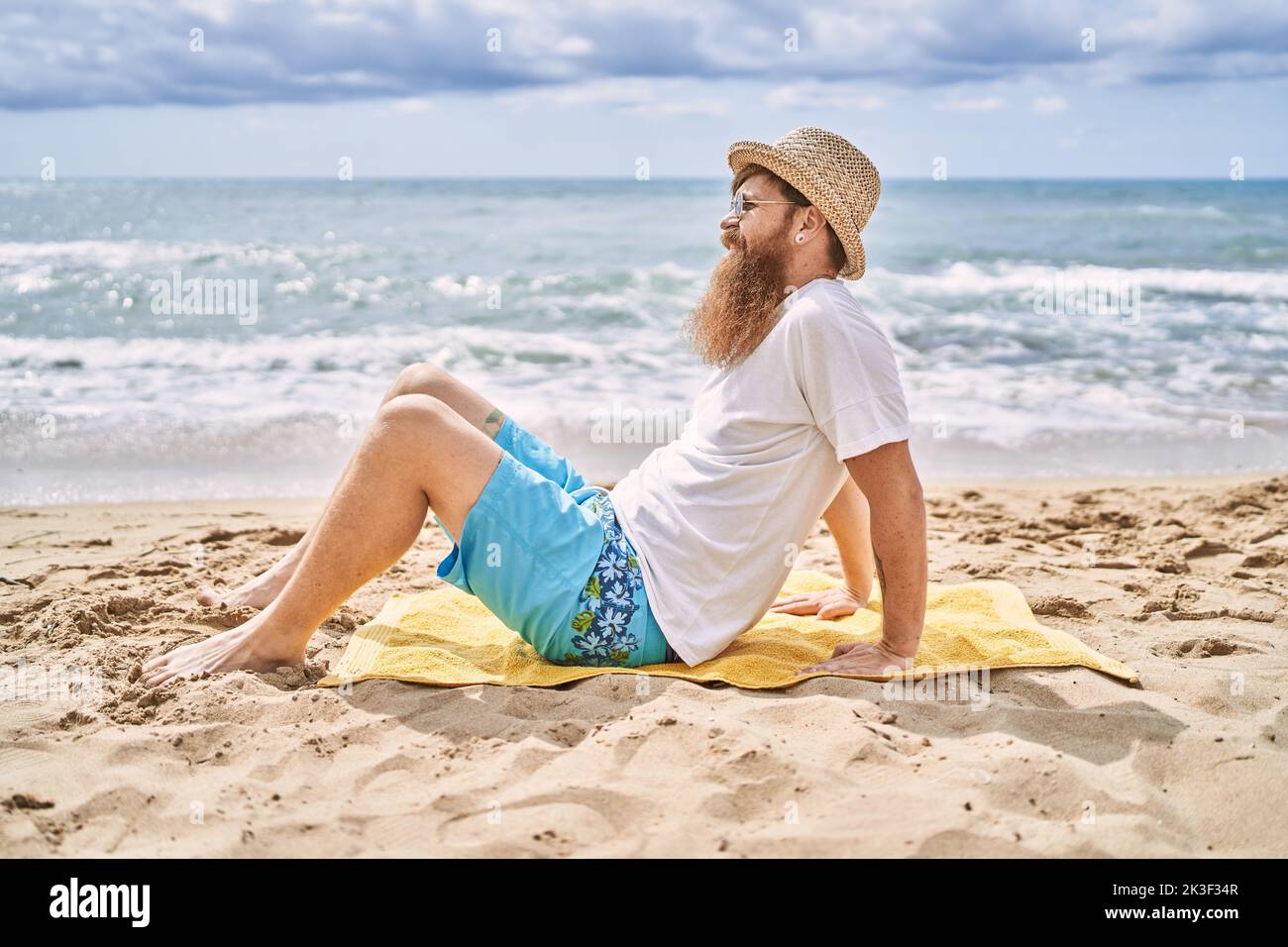 Young redhead man smiling happy sitting on the towel at the beach Stock ...