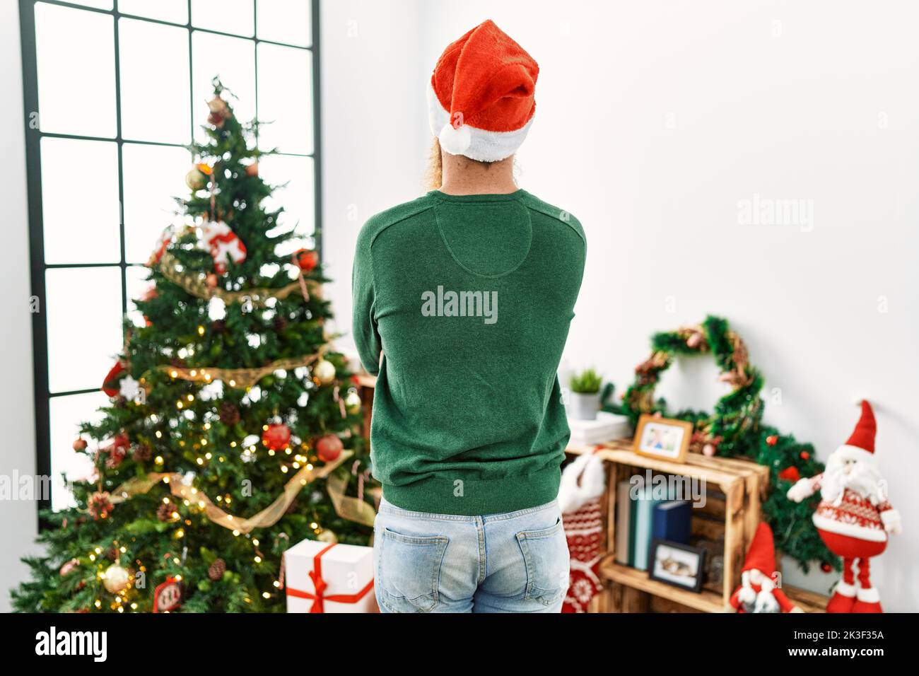 Redhead man with long beard wearing christmas hat by christmas tree ...