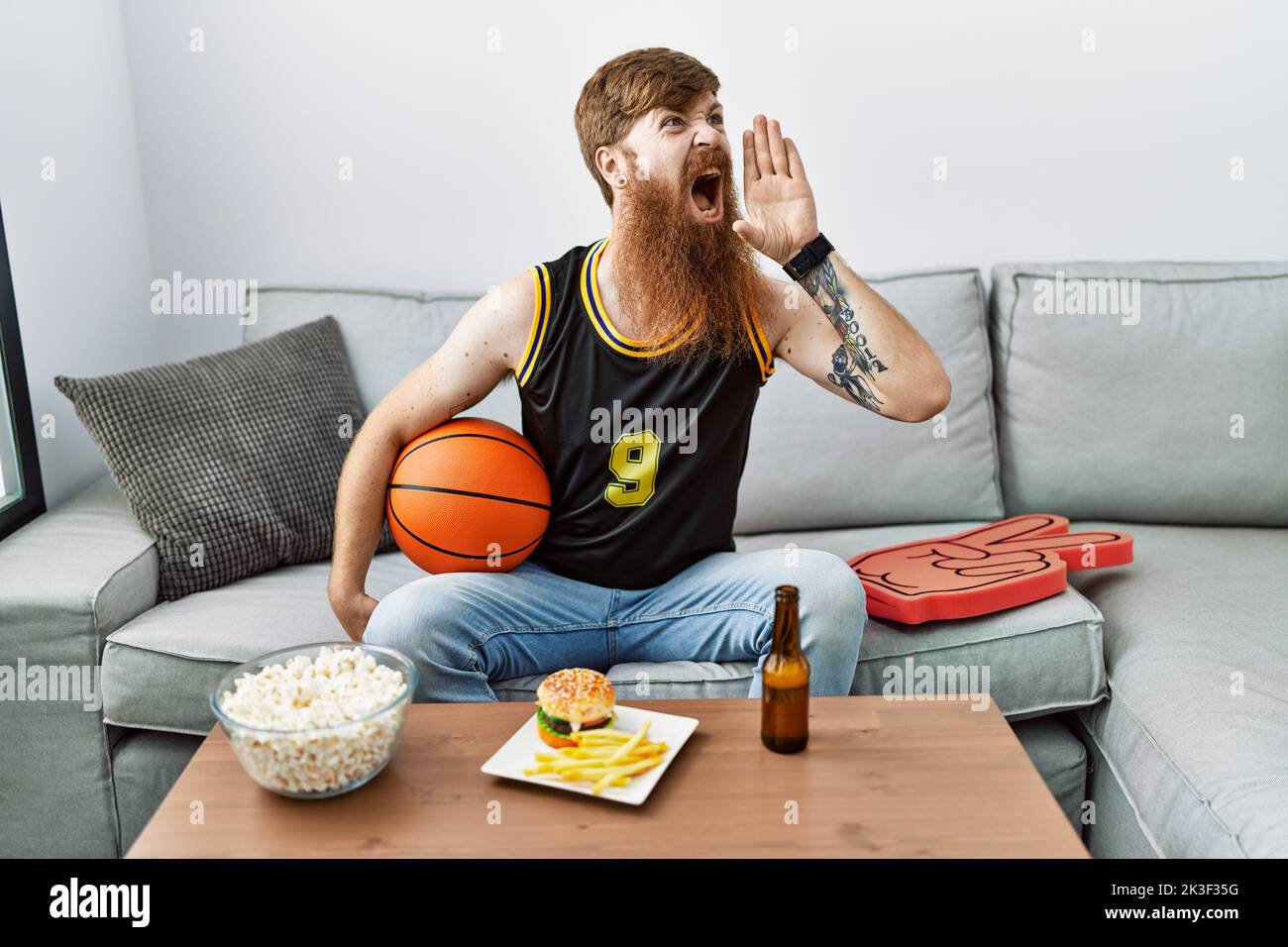 Caucasian man with long beard holding basketball ball cheering tv game ...