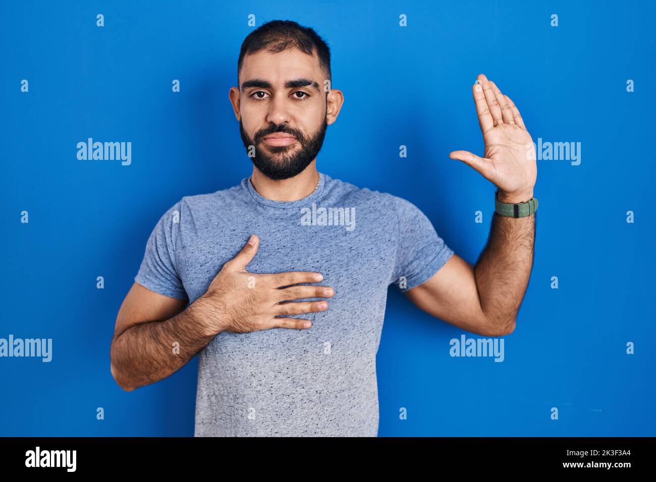 Middle east man with beard standing over blue background swearing with ...