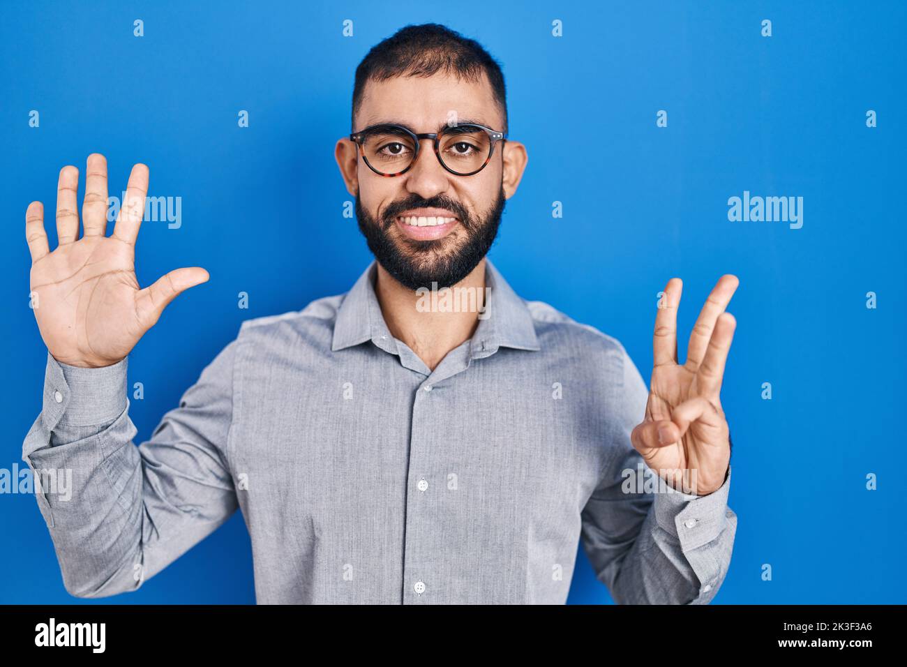 Middle east man with beard standing over blue background showing and ...
