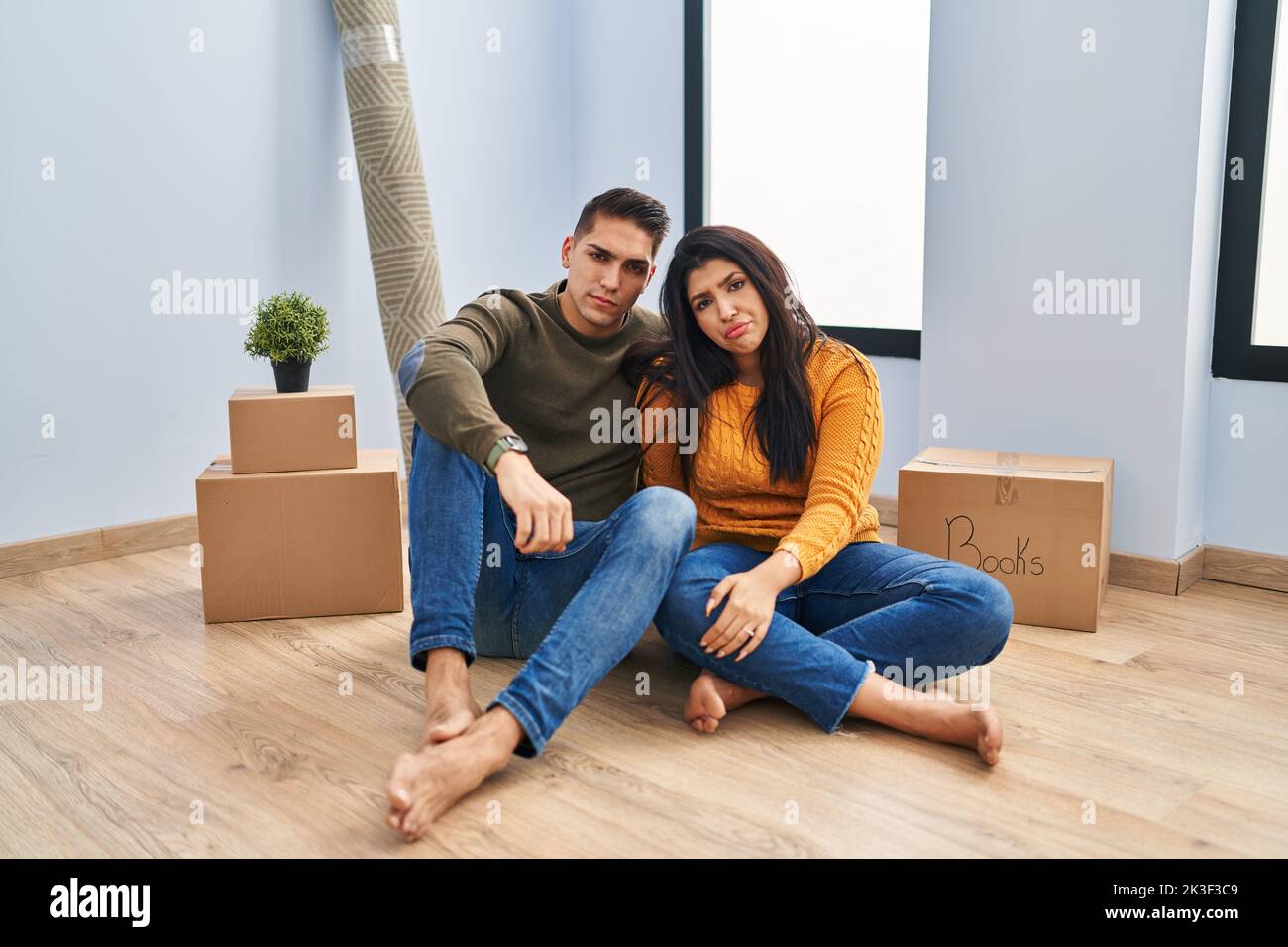 Young couple sitting on the floor at new home depressed and worry for ...
