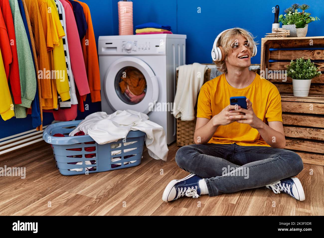 Young blond man listening to music waiting for washing machine at ...
