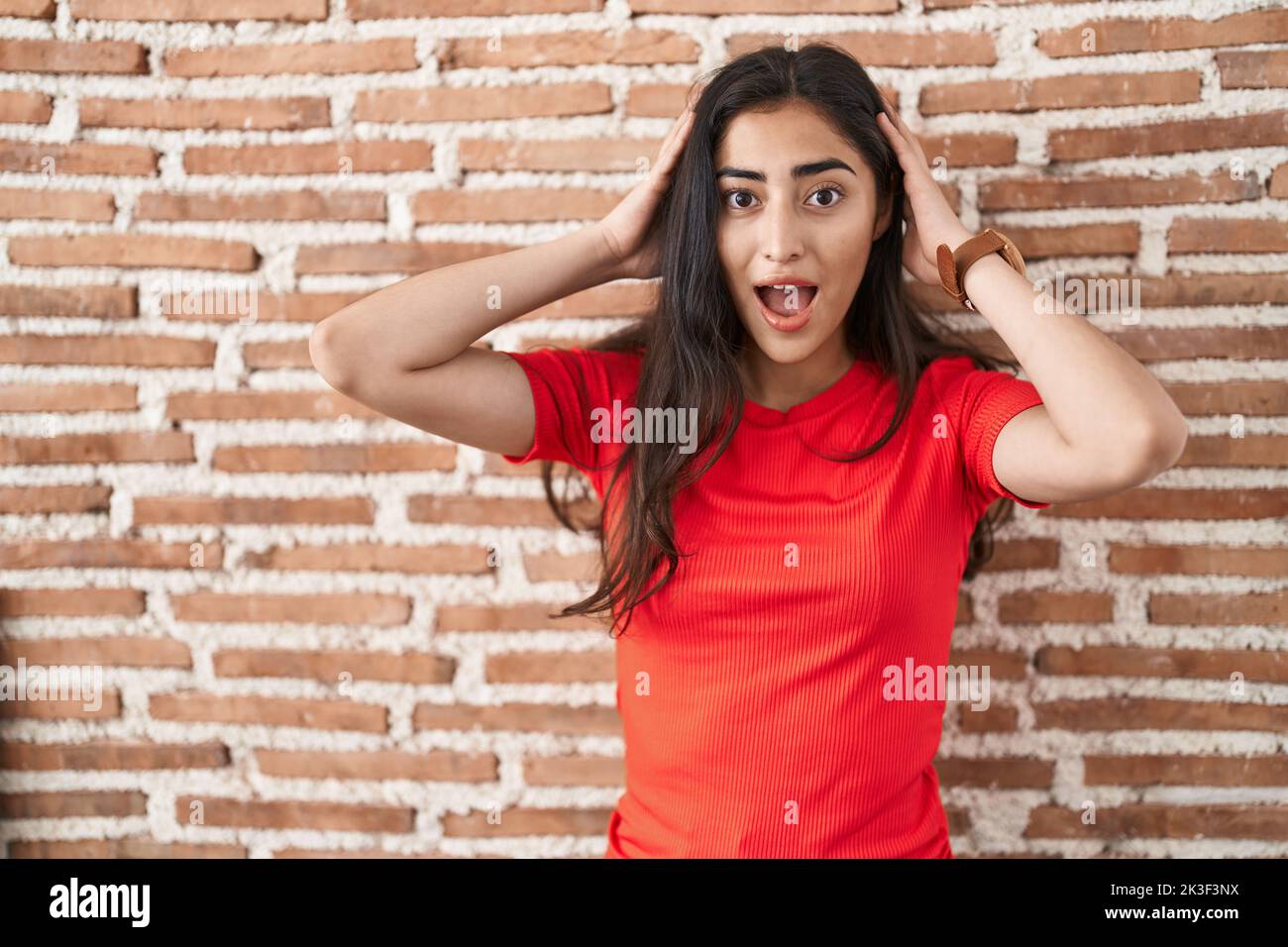 Young teenager girl standing over bricks wall crazy and scared with ...
