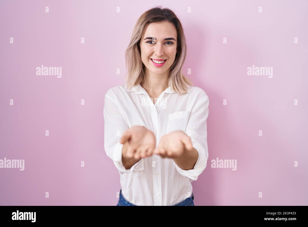 Young beautiful woman standing over pink background smiling with hands ...