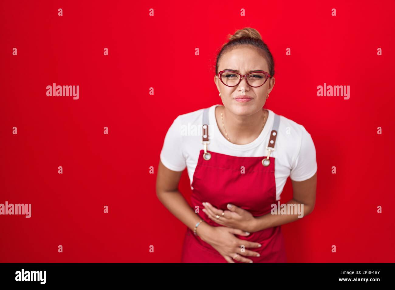 Young hispanic woman wearing waitress apron over red background with ...