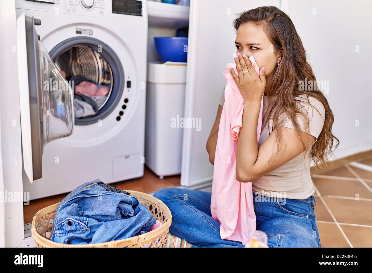 Young hispanic girl doing laundry smelling clean clothes at home Stock ...