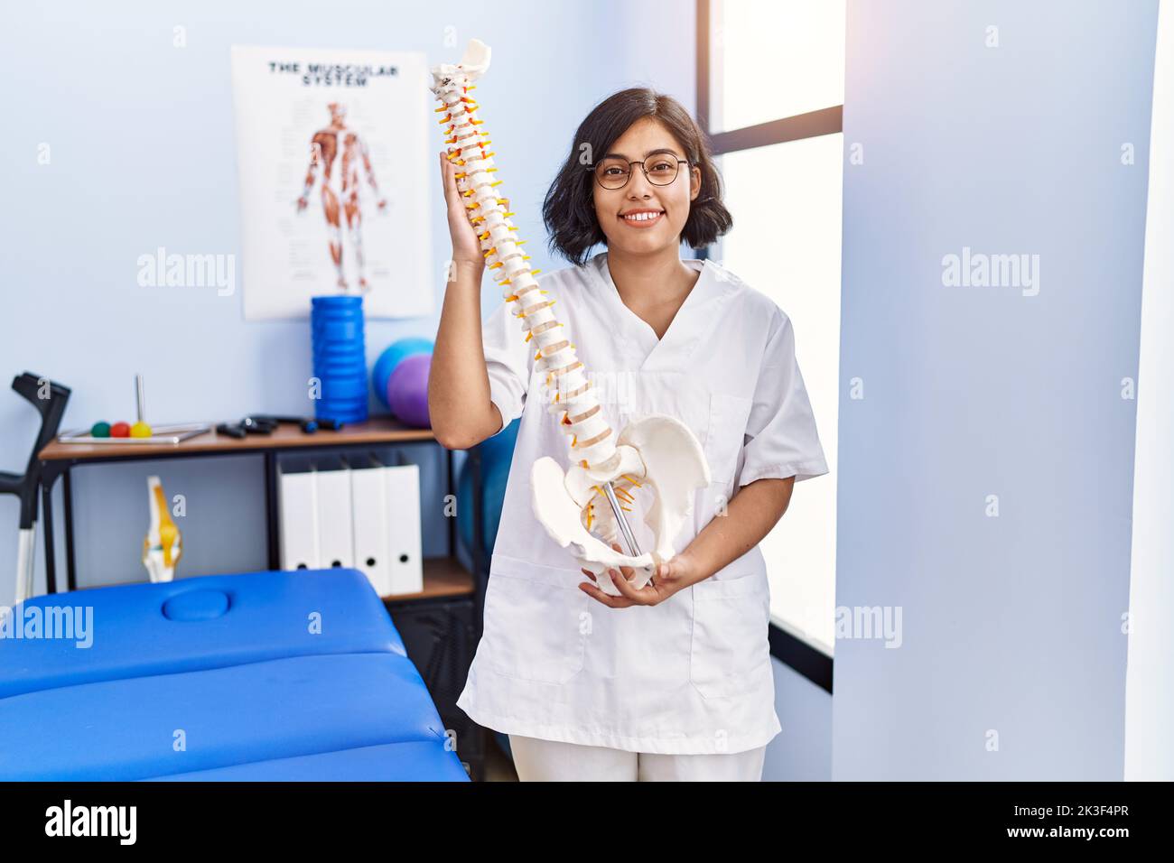 Young latin woman wearing physiotherapist uniform holding anatomical ...