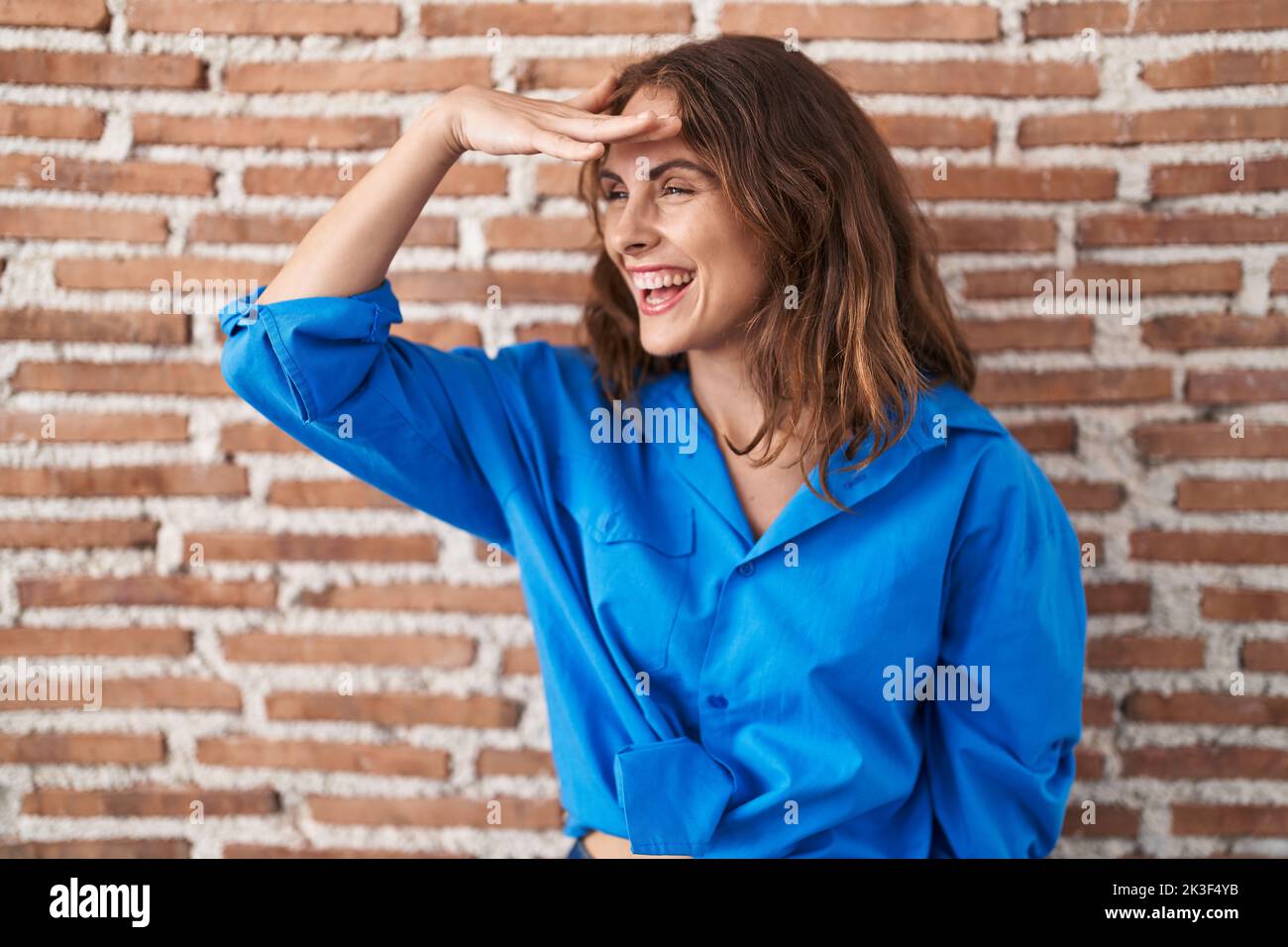 Beautiful brunette woman standing over bricks wall very happy and ...