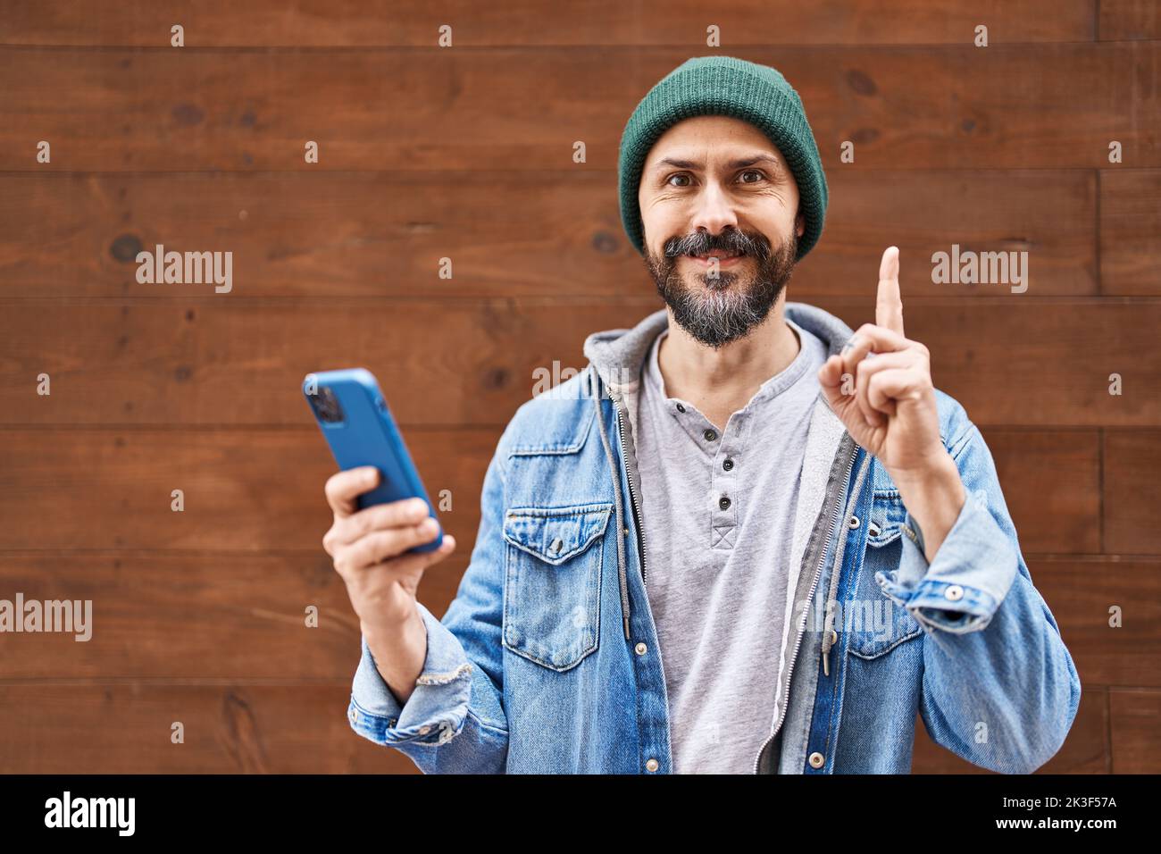 Young hispanic man using smartphone surprised with an idea or question ...