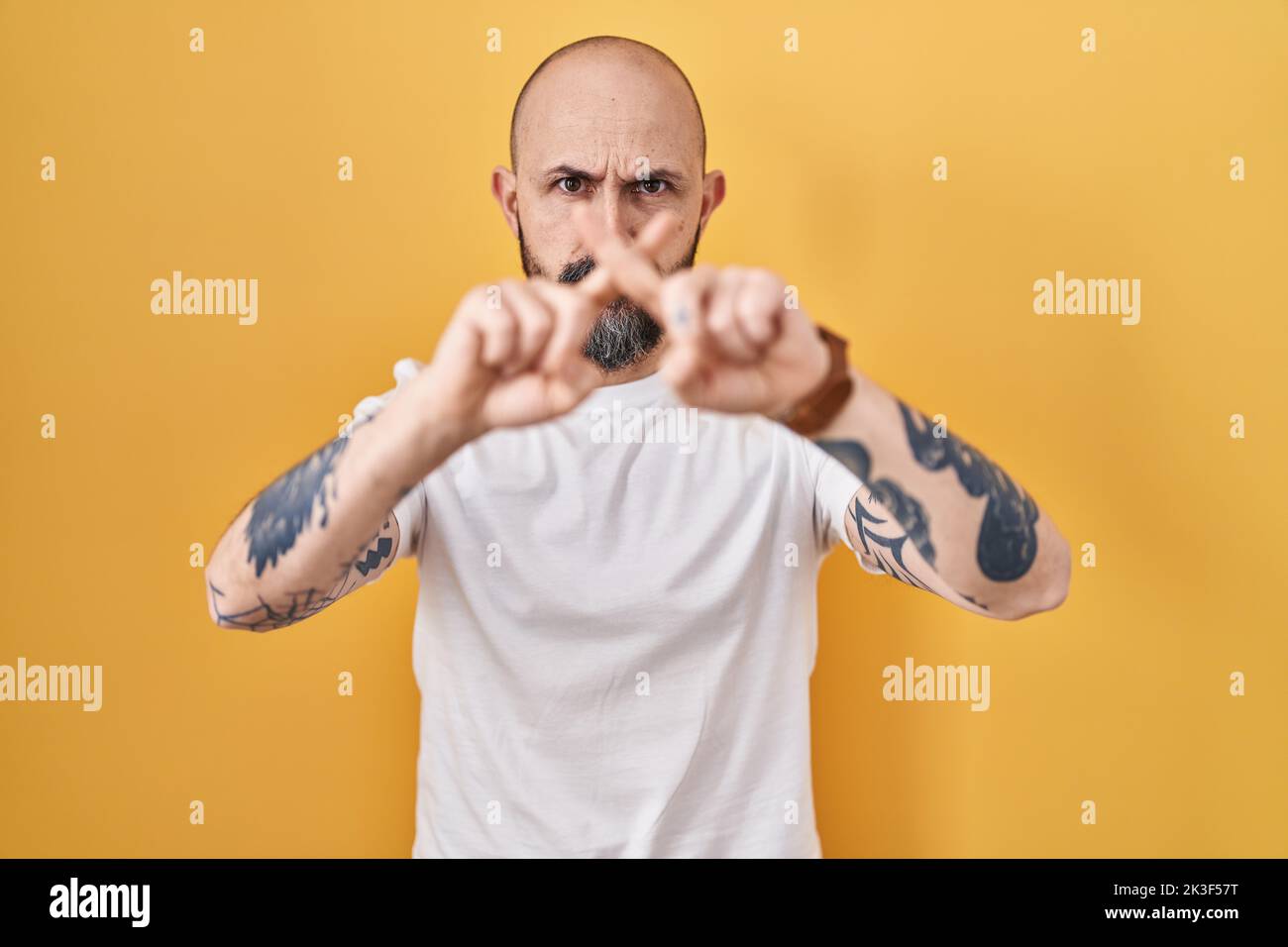 Young hispanic man with tattoos standing over yellow background ...