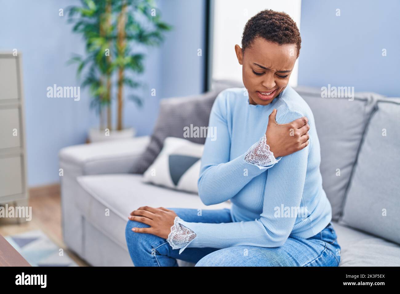 African american woman sitting on sofa suffering for shoulder pain at ...