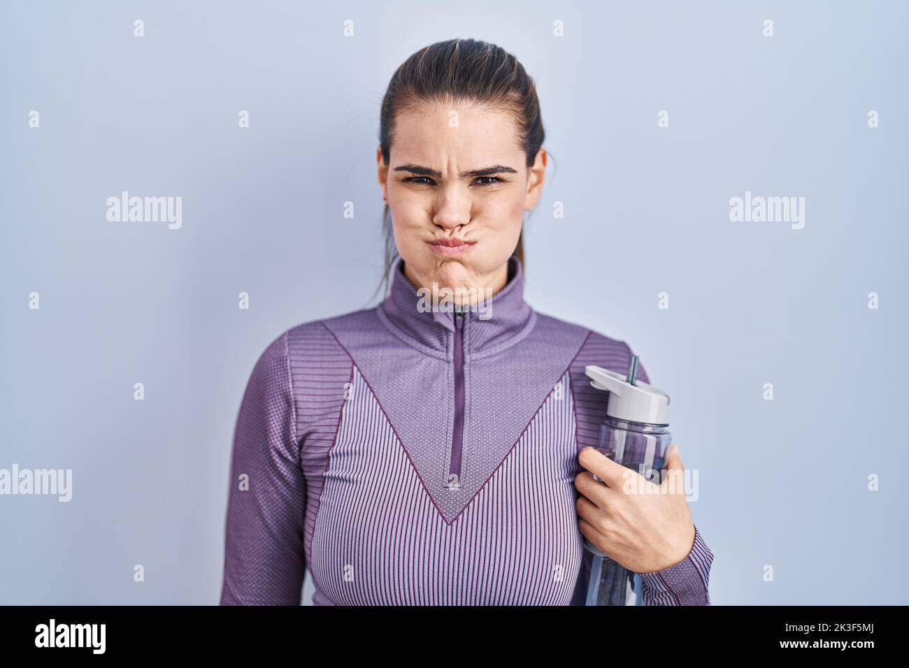 Beautiful woman wearing sportswear holding water bottle puffing cheeks ...