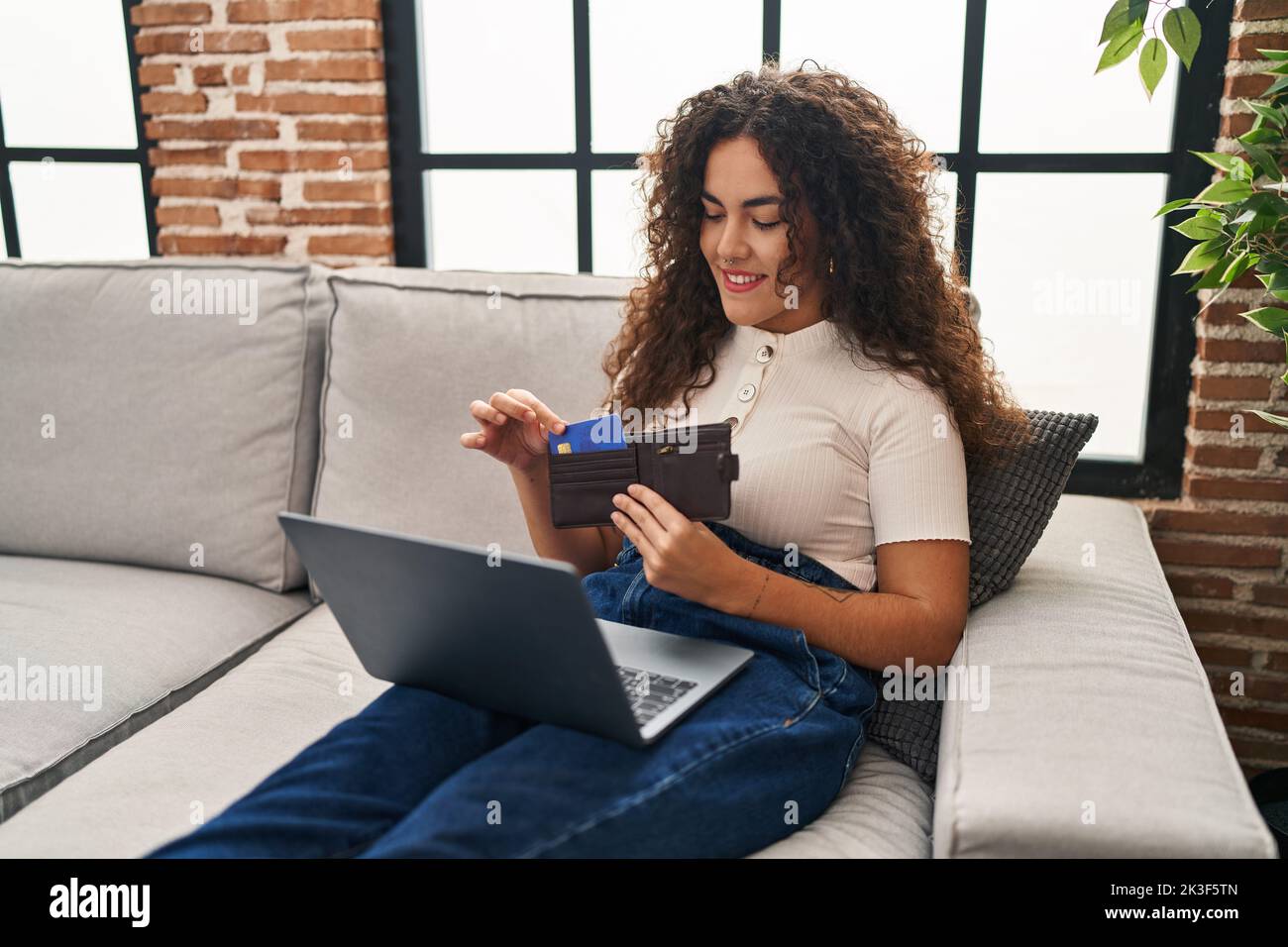 Young beautiful hispanic woman using laptop holding credit card sitting ...