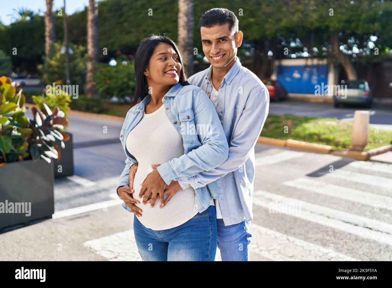 Young latin couple expecting baby hugging each other standing at street Stock Photo - Alamy