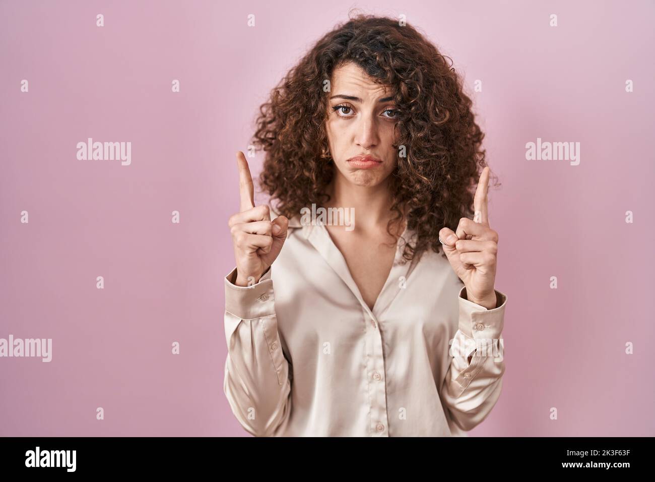 Hispanic woman with curly hair standing over pink background pointing ...