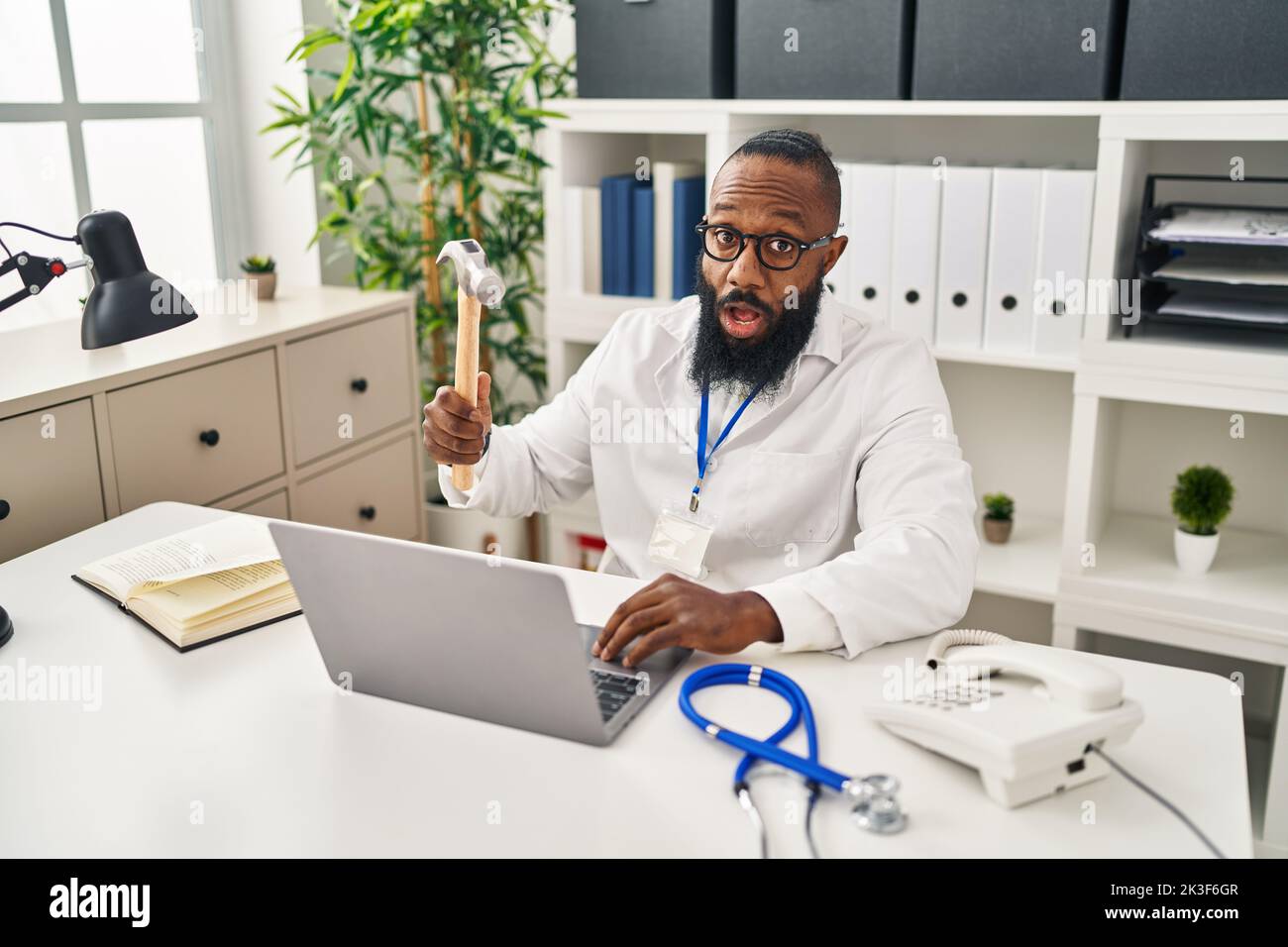 African american man working at medical clinic holding hammer scared ...