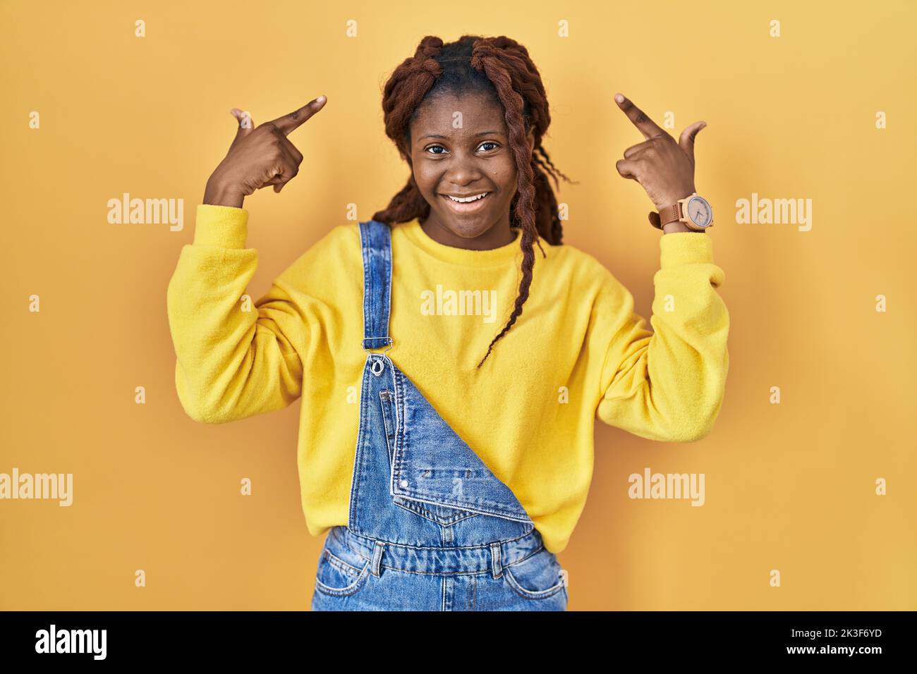 African woman standing over yellow background smiling pointing to head ...