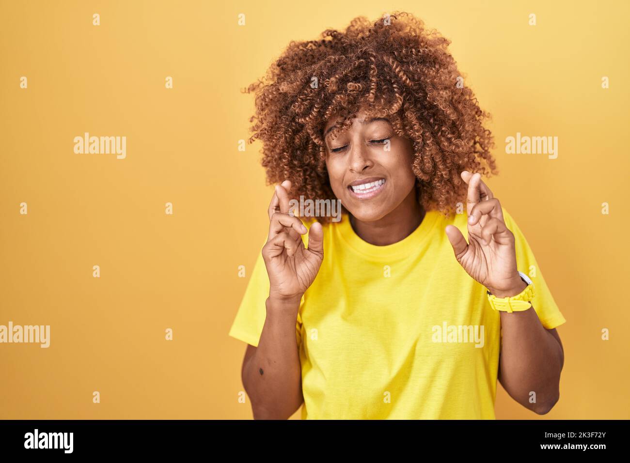 Young hispanic woman with curly hair standing over yellow background ...