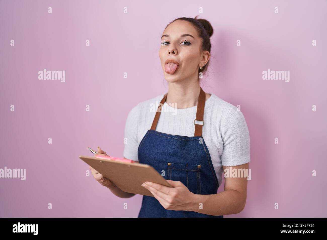 Young hispanic girl wearing professional waitress apron taking order ...