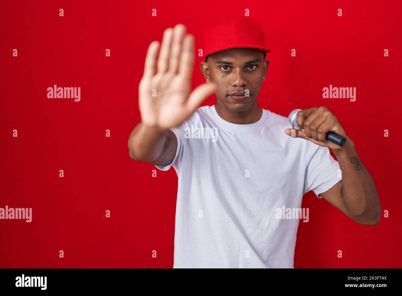 Young hispanic man singing song using microphone with open hand doing ...