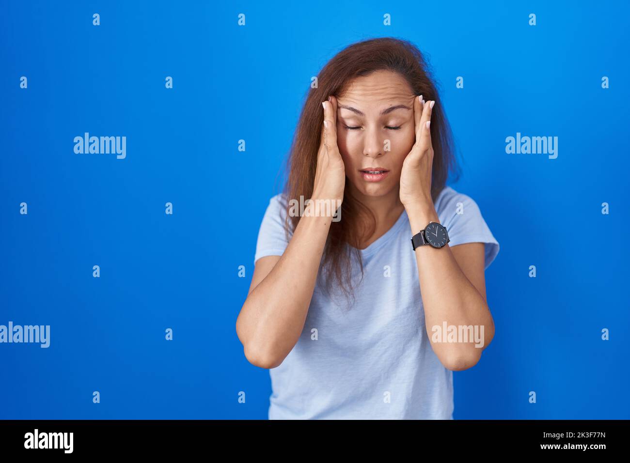 Brunette woman standing over blue background with hand on head ...