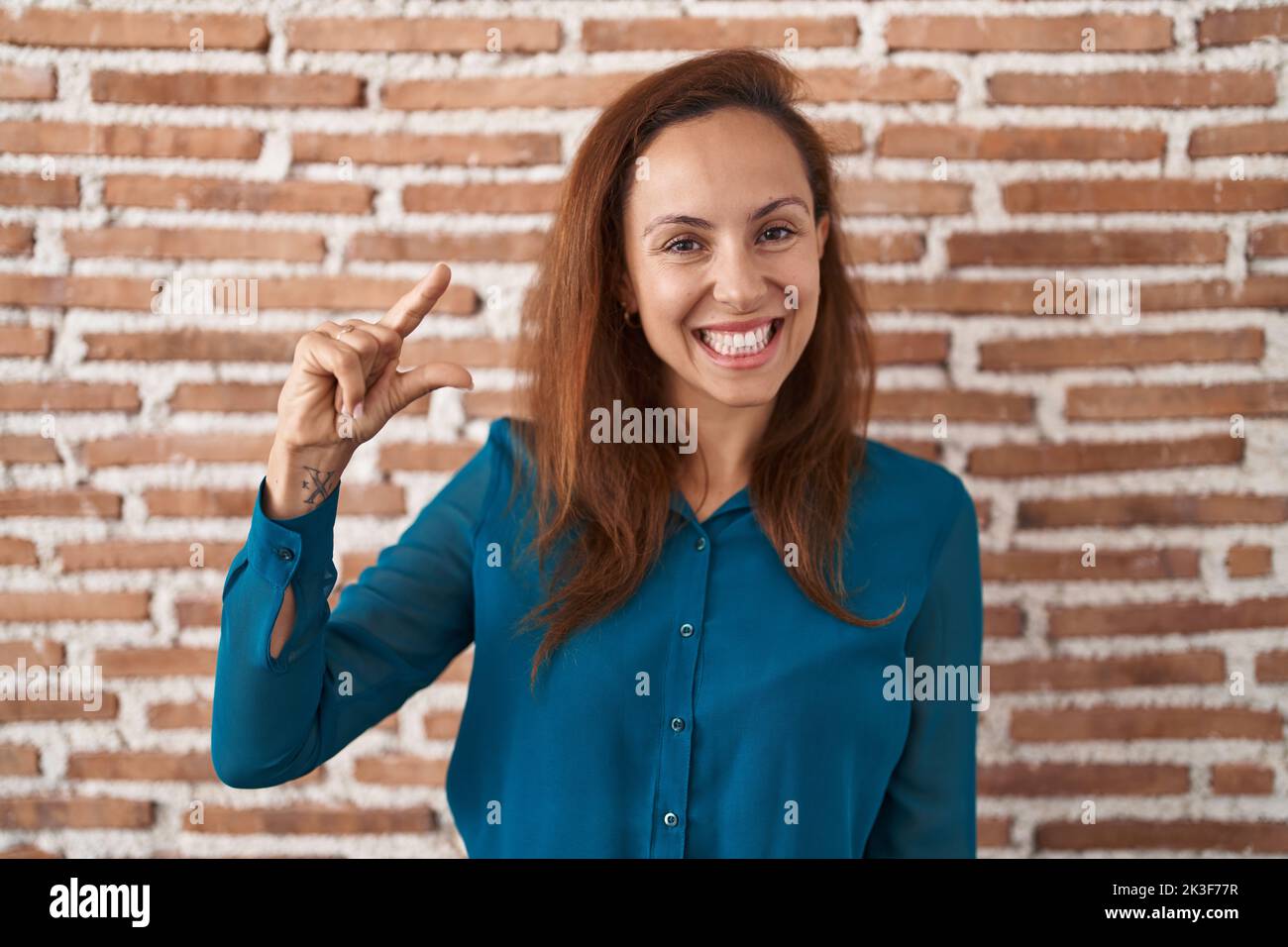 Brunette woman standing over bricks wall smiling and confident ...