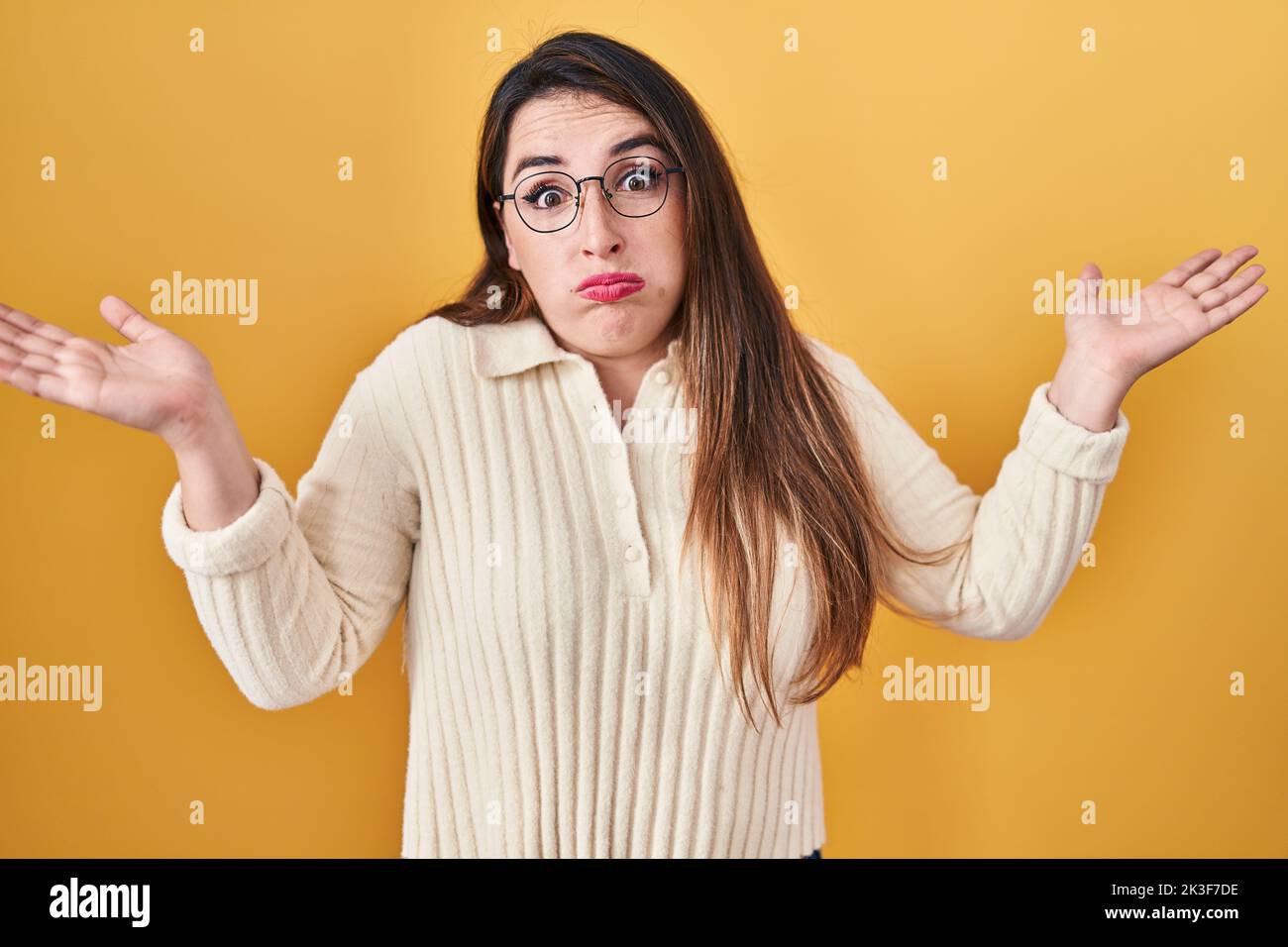 Young hispanic woman standing over yellow background clueless and ...