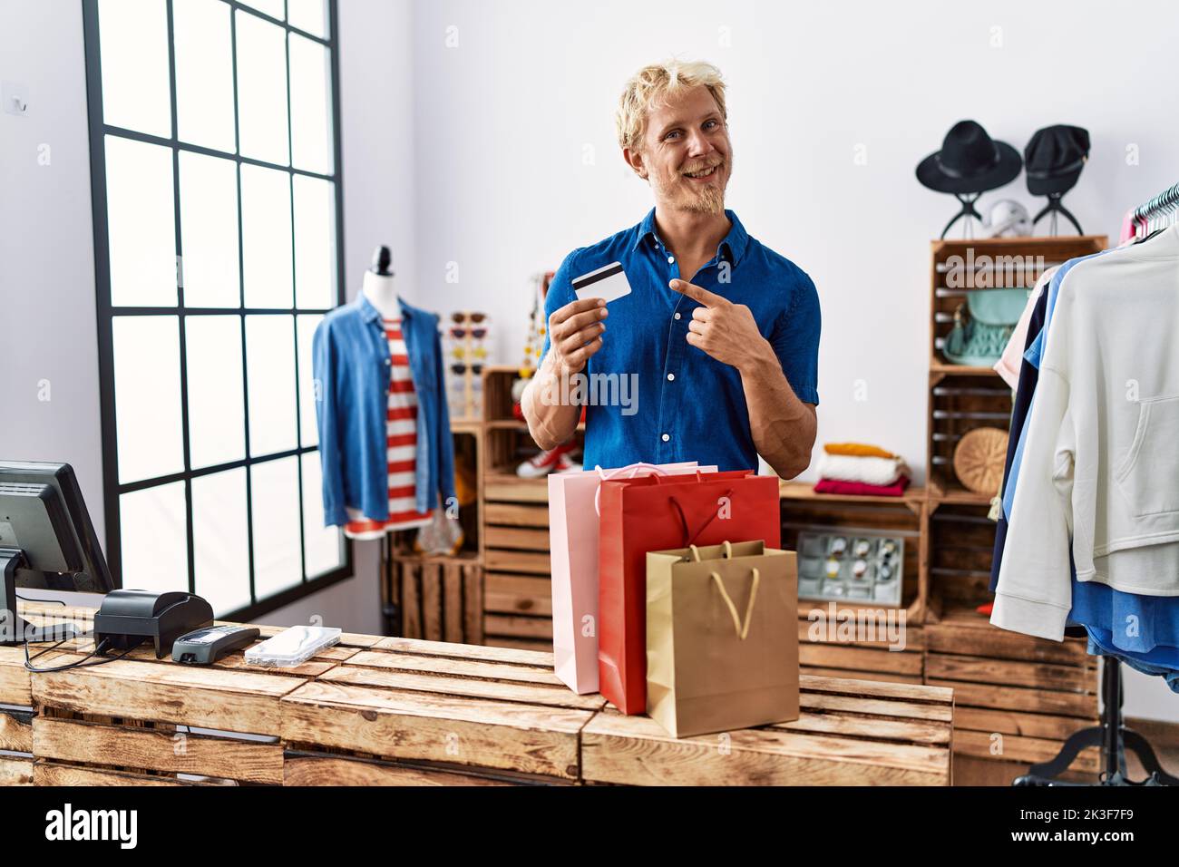 Young blond man holding credit card working as manager at retail ...
