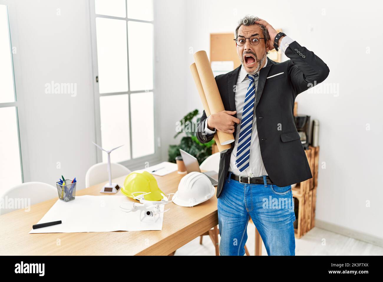 Middle age hispanic business man holding paper blueprints crazy and ...