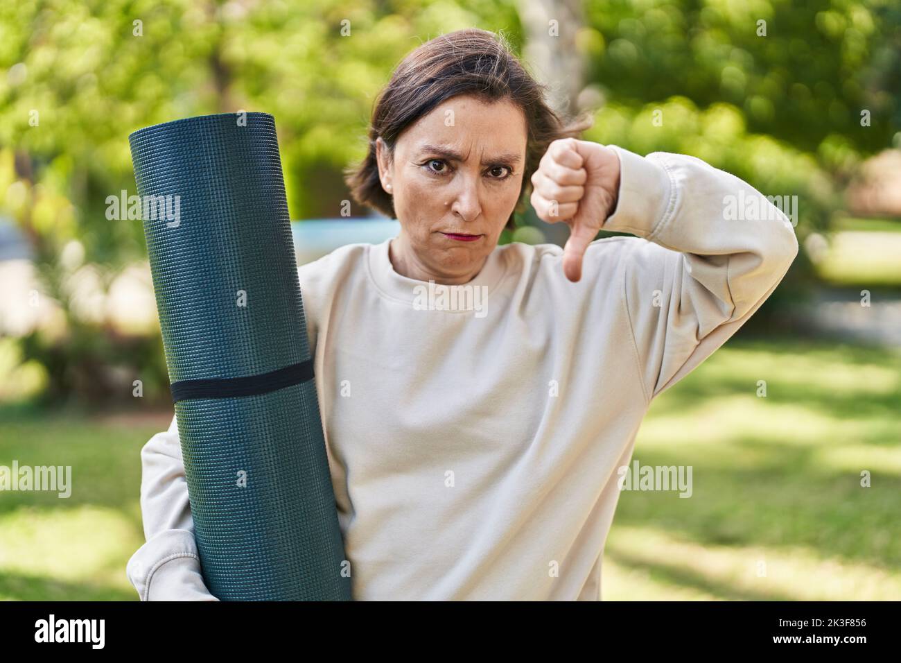 Middle age hispanic woman holding yoga mat at the park with angry face ...