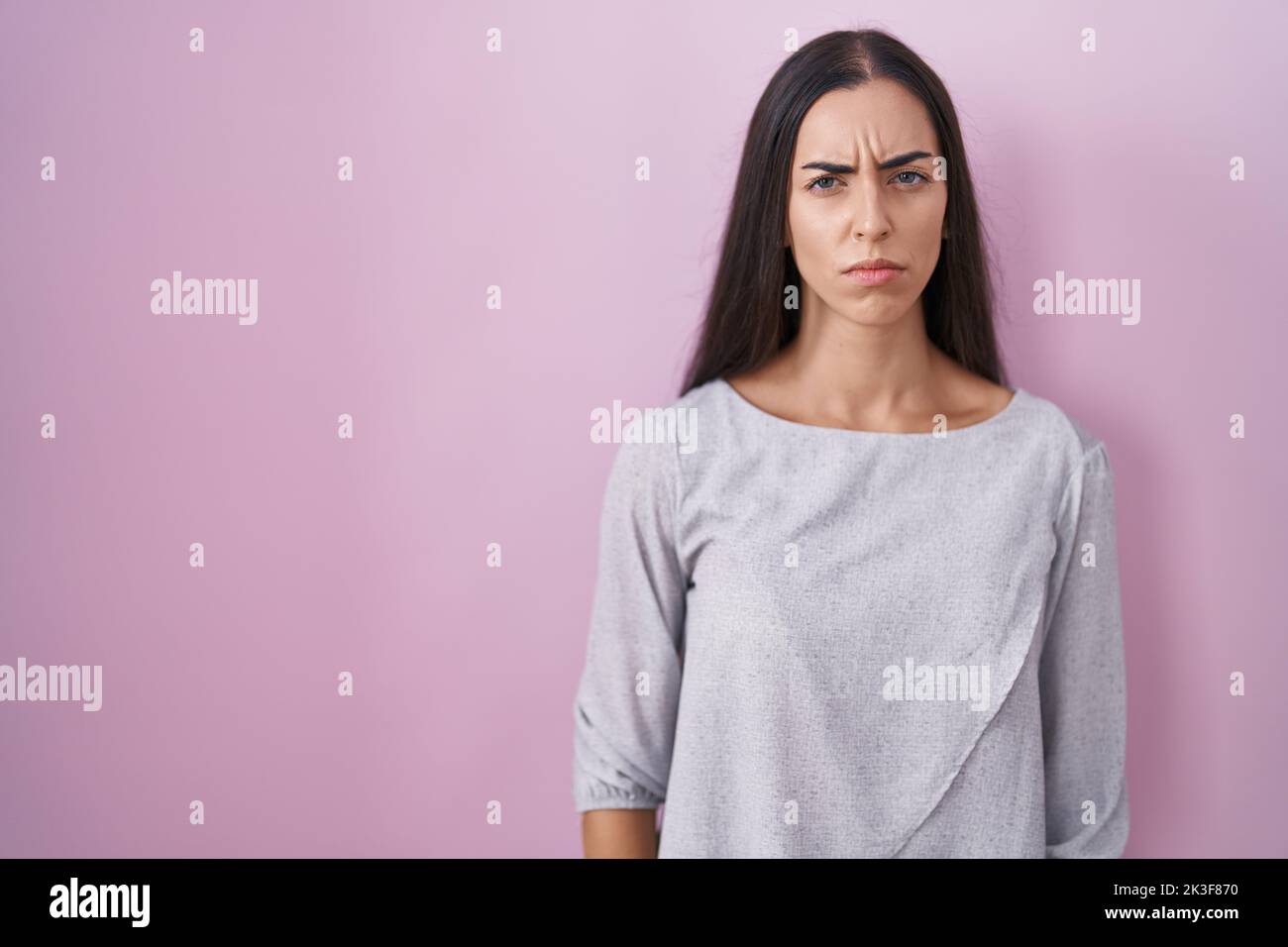 Young brunette woman standing over pink background skeptic and nervous ...