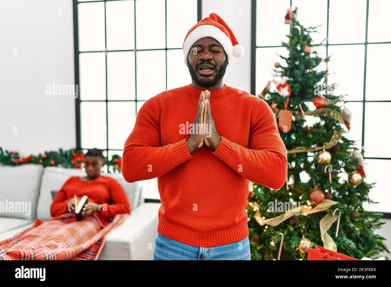 Young african american man standing by christmas tree begging and ...