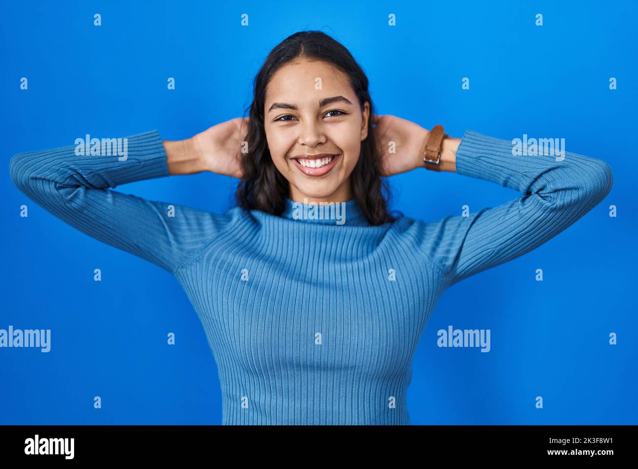 Young brazilian woman standing over blue isolated background relaxing ...