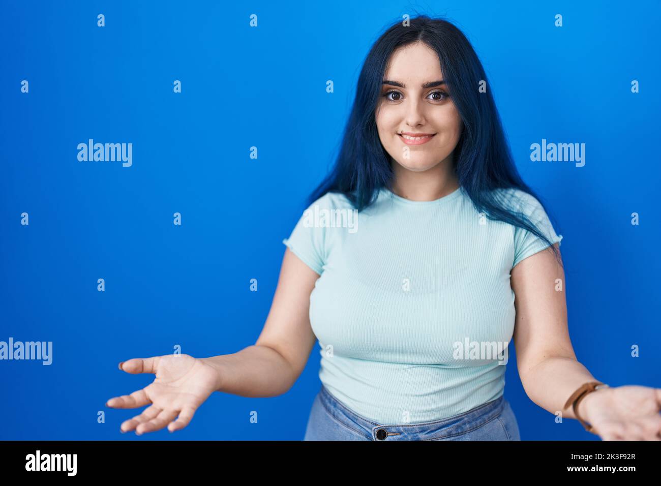 Young modern girl with blue hair standing over blue background smiling ...