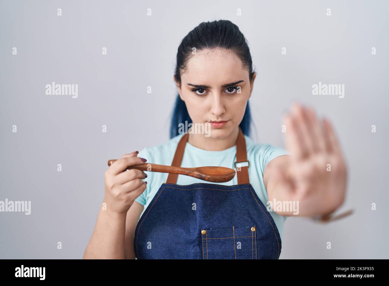 Young modern girl with blue hair wearing cook apron holding spoon with ...