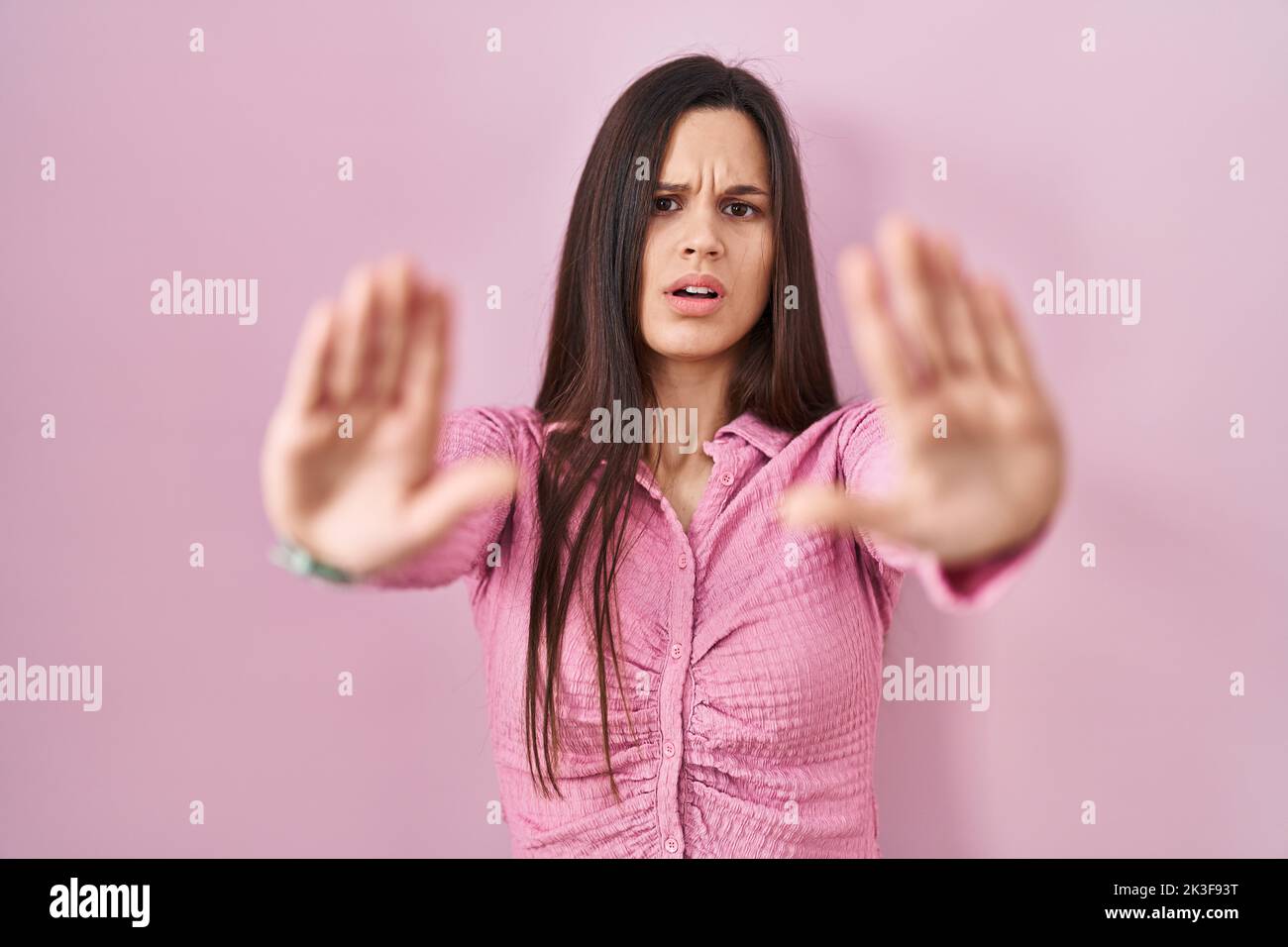 Young hispanic woman standing over pink background doing stop gesture ...