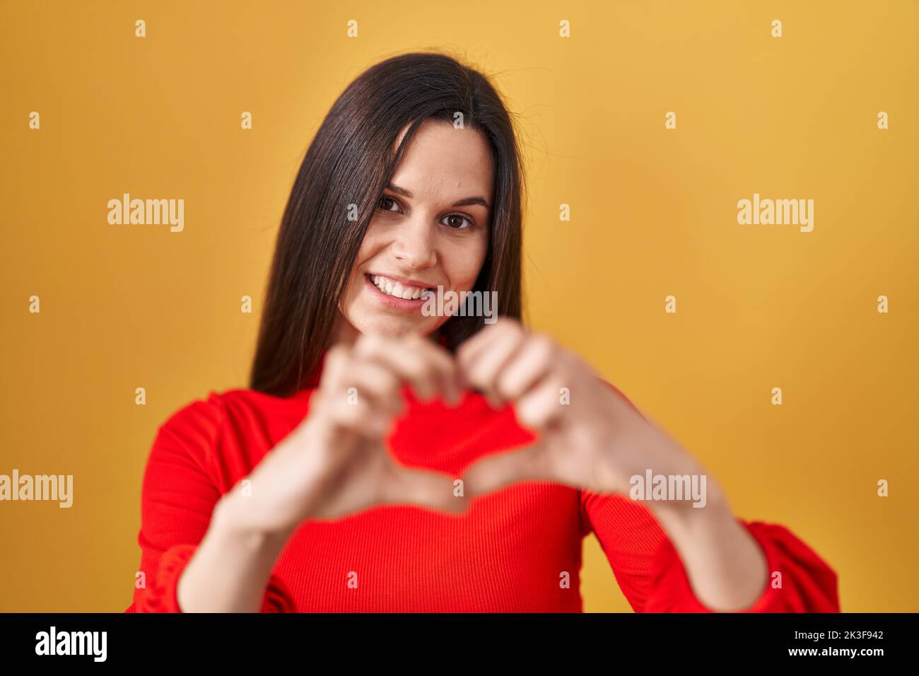 Young hispanic woman standing over yellow background smiling in love ...