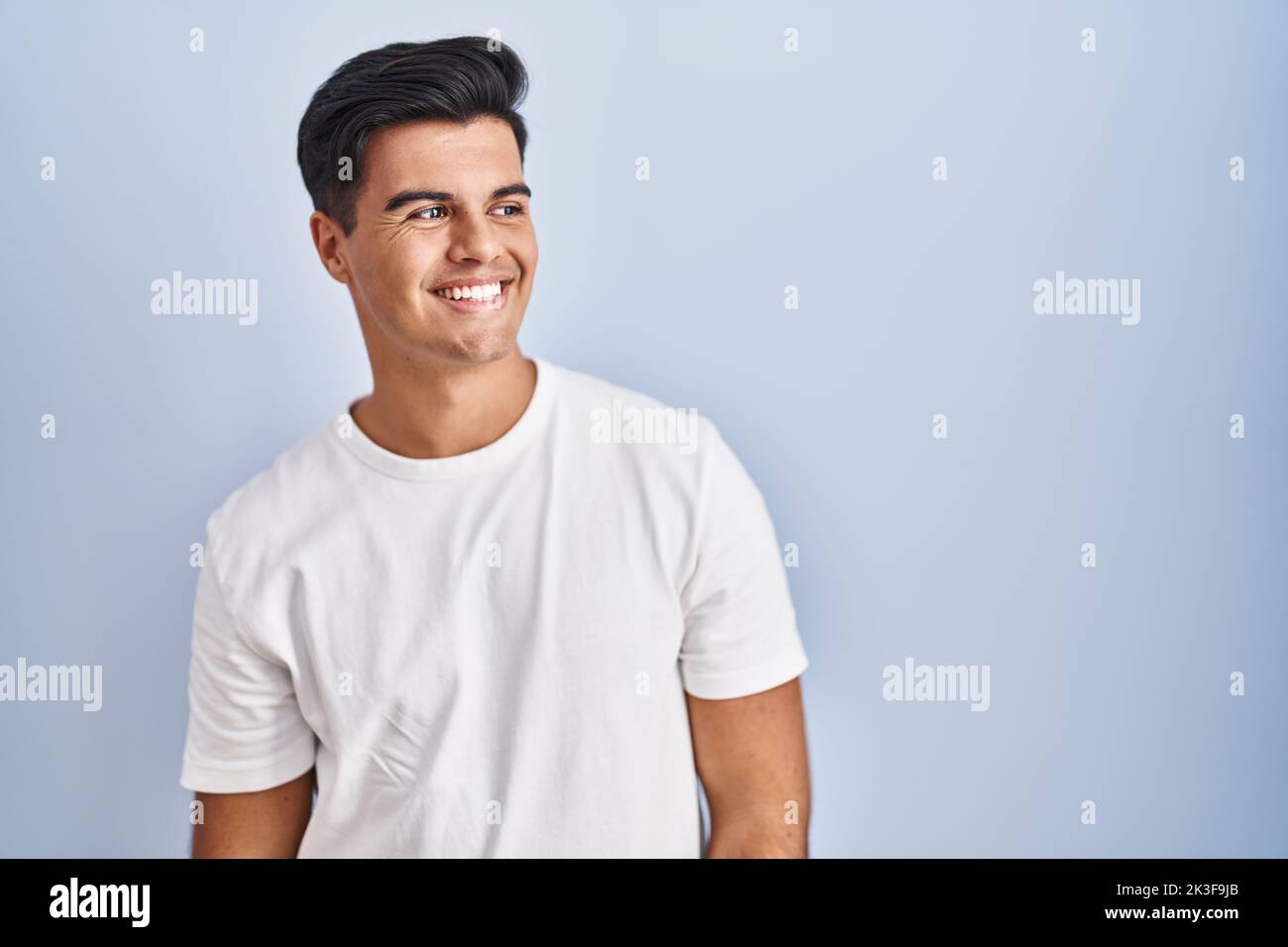 Hispanic man standing over blue background looking away to side with ...
