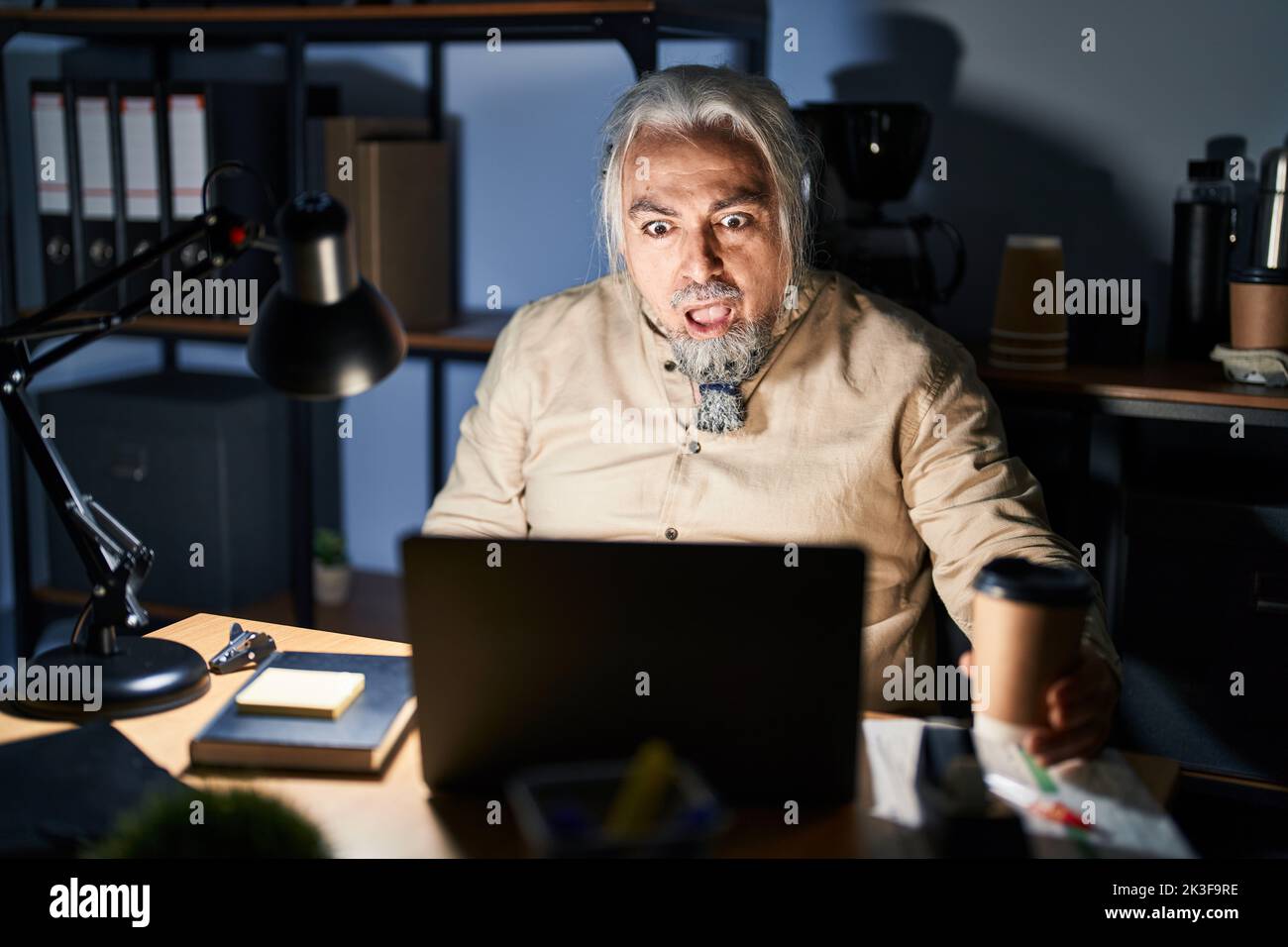 Middle age man with grey hair working at the office at night in shock ...