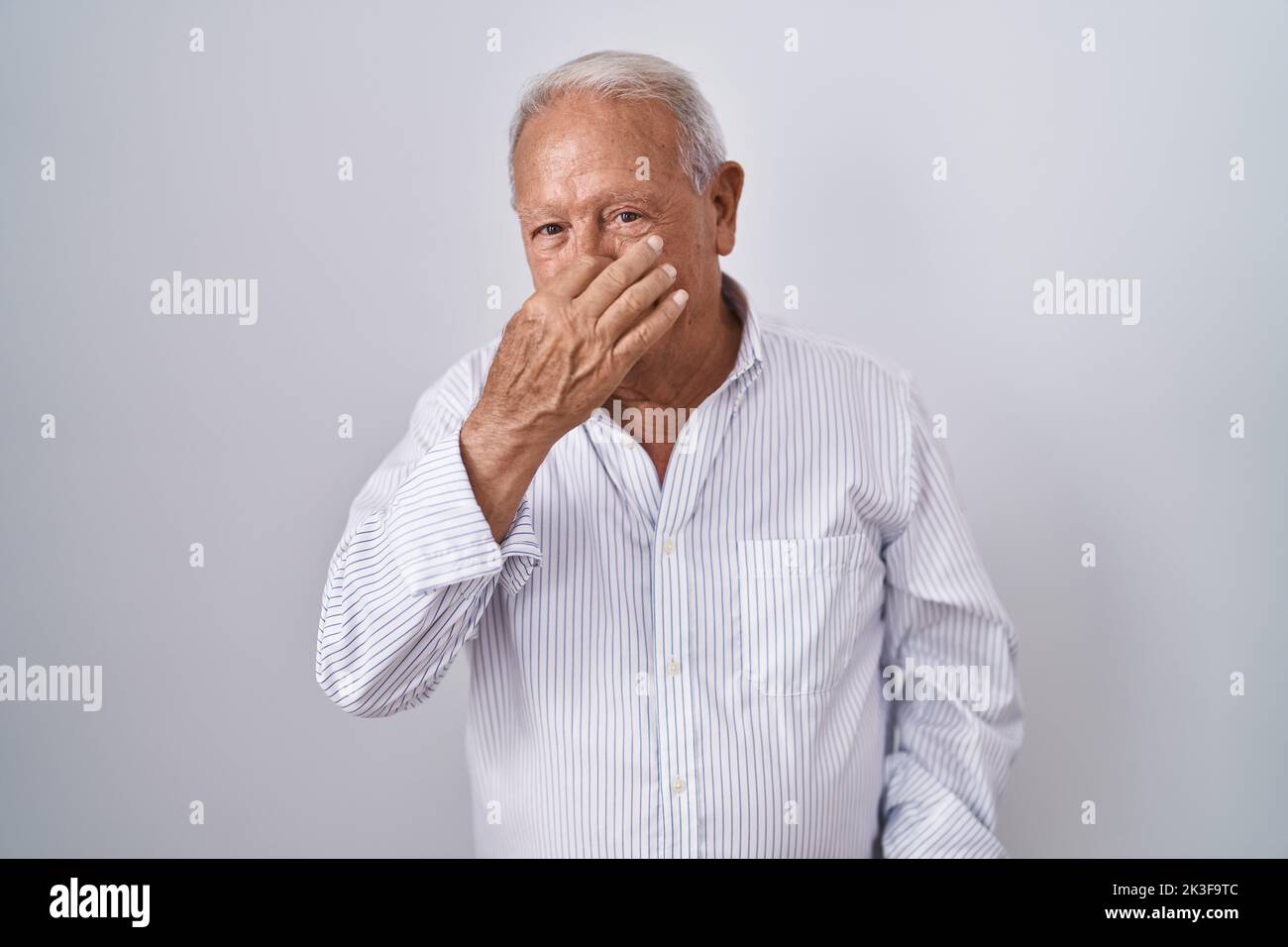 Senior man with grey hair standing over isolated background smelling ...