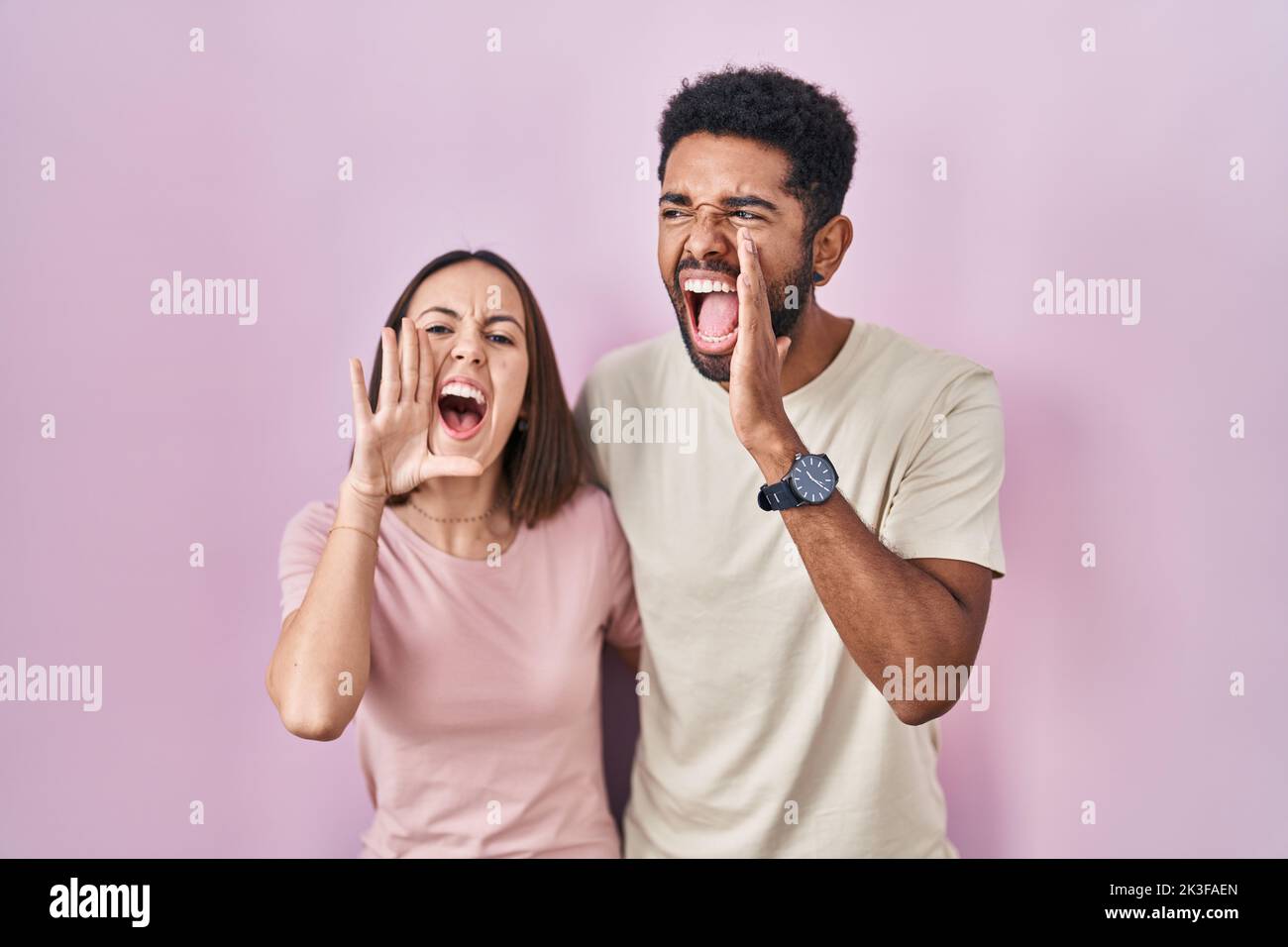 Young hispanic couple together over pink background shouting and ...