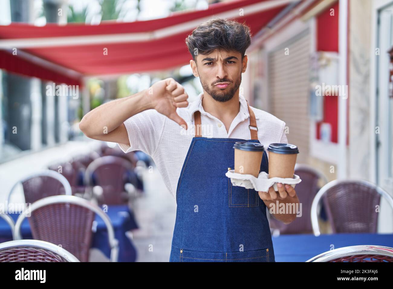 Arab man with beard wearing waiter apron at restaurant terrace with ...
