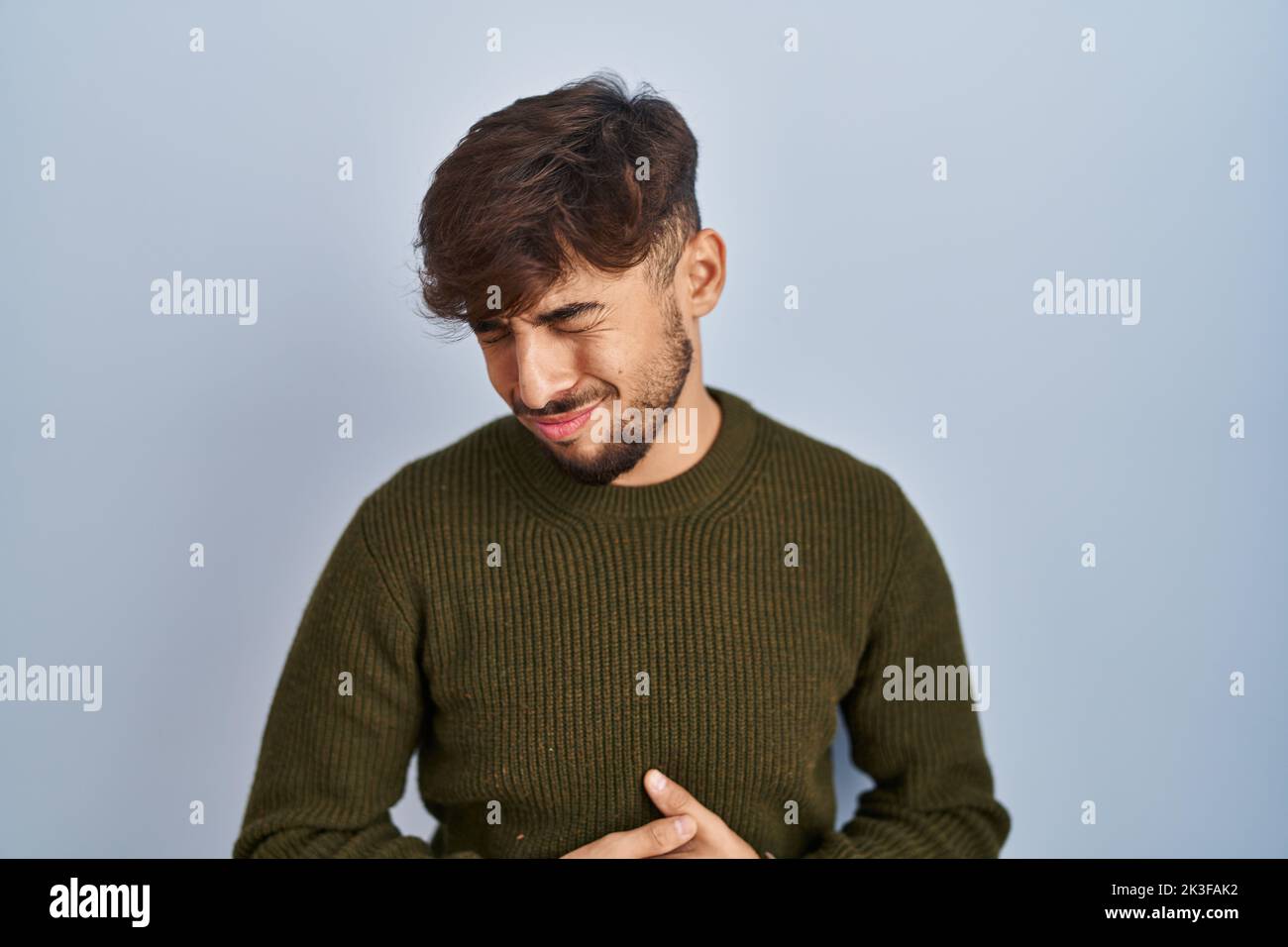 Arab man with beard standing over blue background with hand on stomach ...