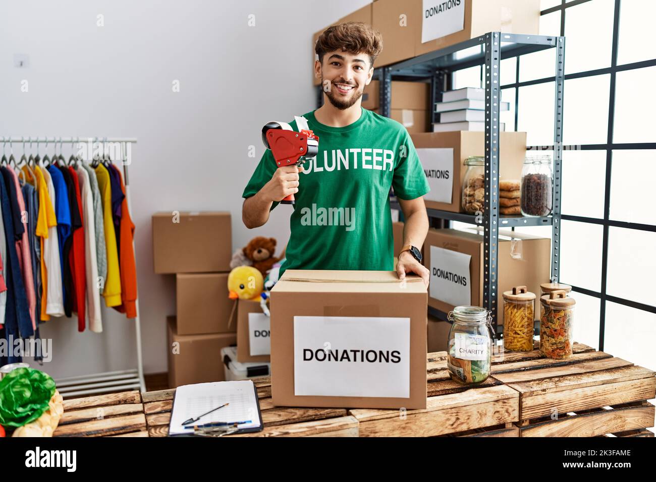 Young arab man wearing volunteer uniform packing donations box at ...