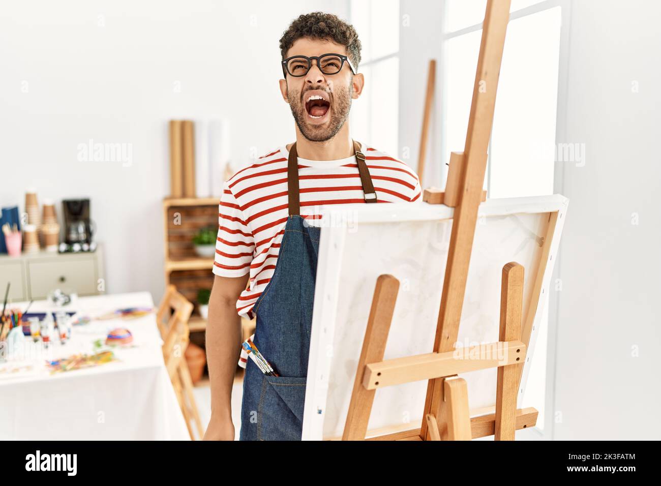 Arab young man at art studio angry and mad screaming frustrated and ...